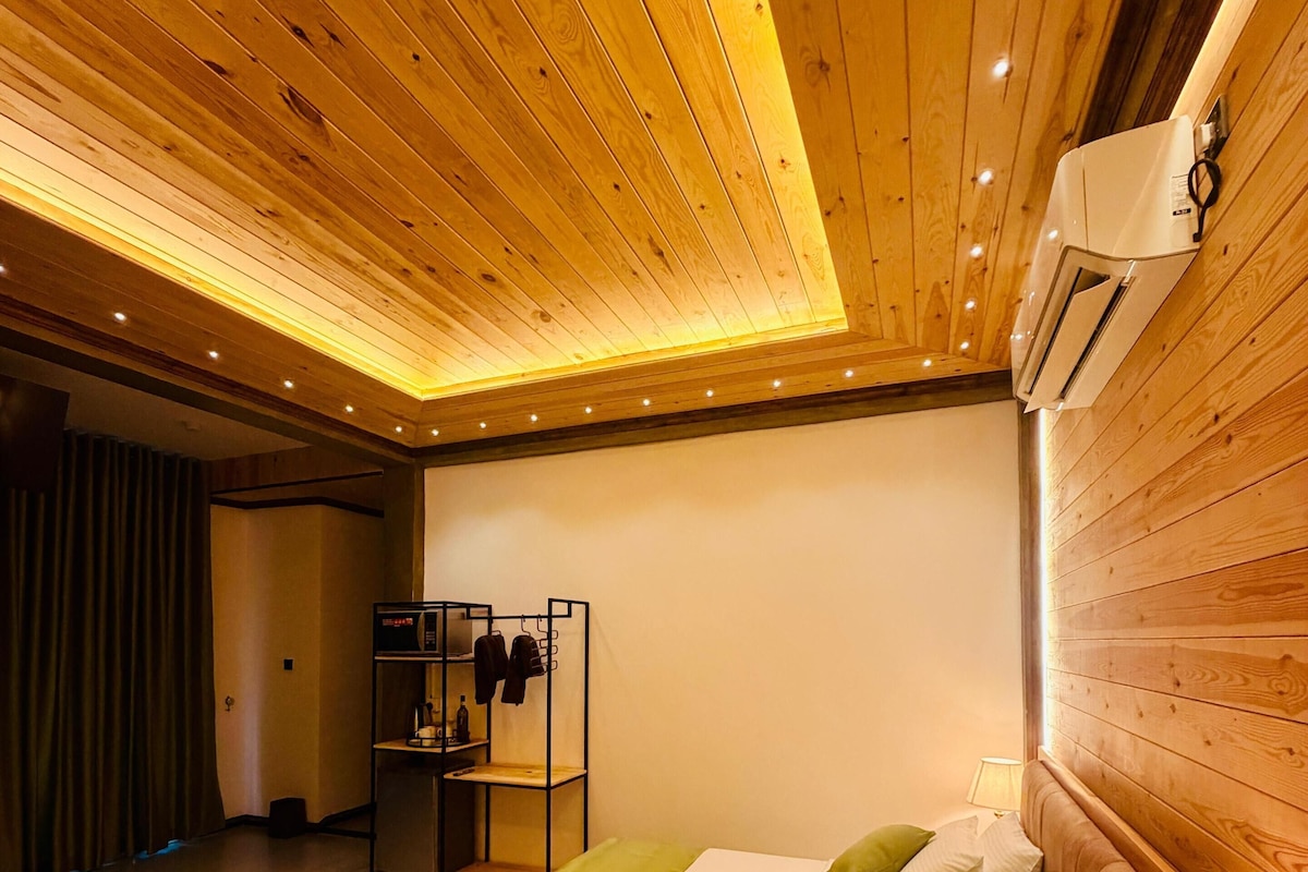 Quarto de hotel com duas camas, teto de madeira, ar condicionado e prateleira com roupas.