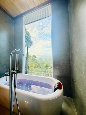 Uma banheira com vista para vegetação e montanhas através de uma janela.