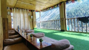 Quarto com uma longa mesa de madeira, assentos acolchoados e vista para uma paisagem montanhosa.