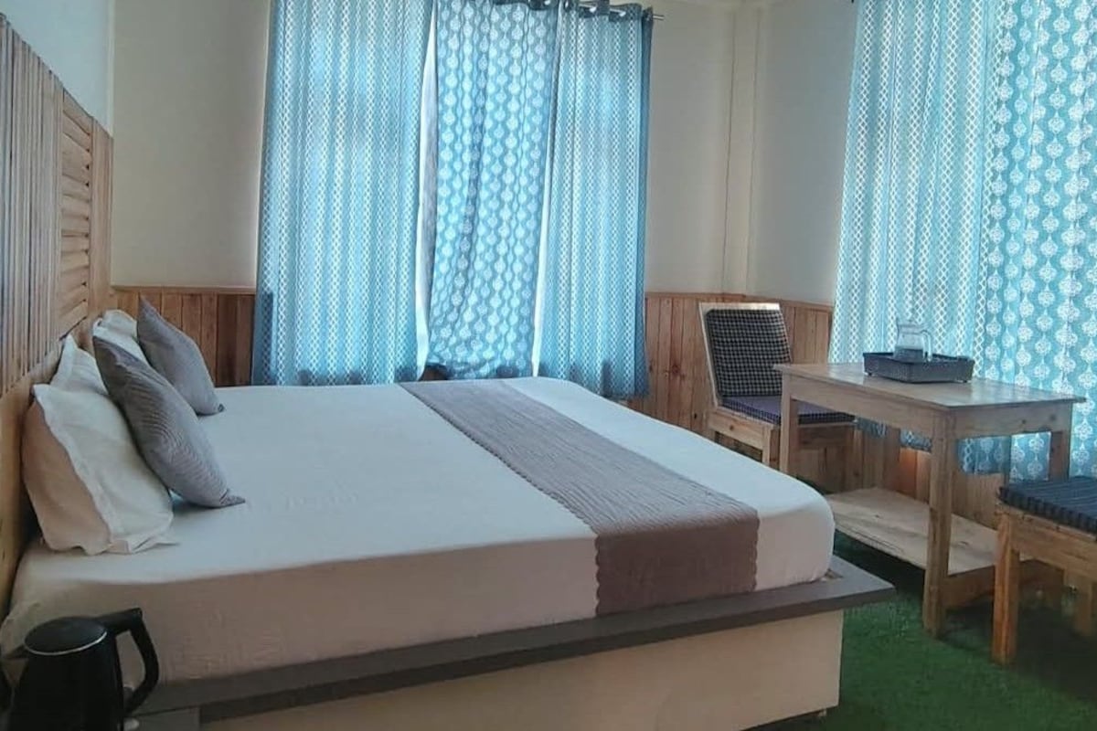 Quarto de hotel com cama, uma mesinha, cadeira e cortinas.