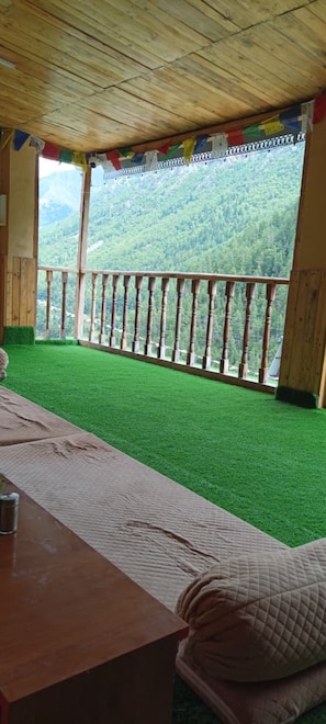 Quarto com teto de madeira, varanda com guarda-corpo e vista para uma paisagem verde.
