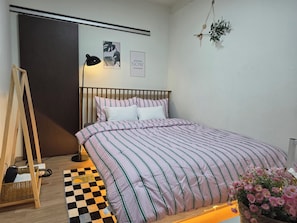 Quarto com cama, luminária de pé, tapete xadrez e obras de arte nas paredes.