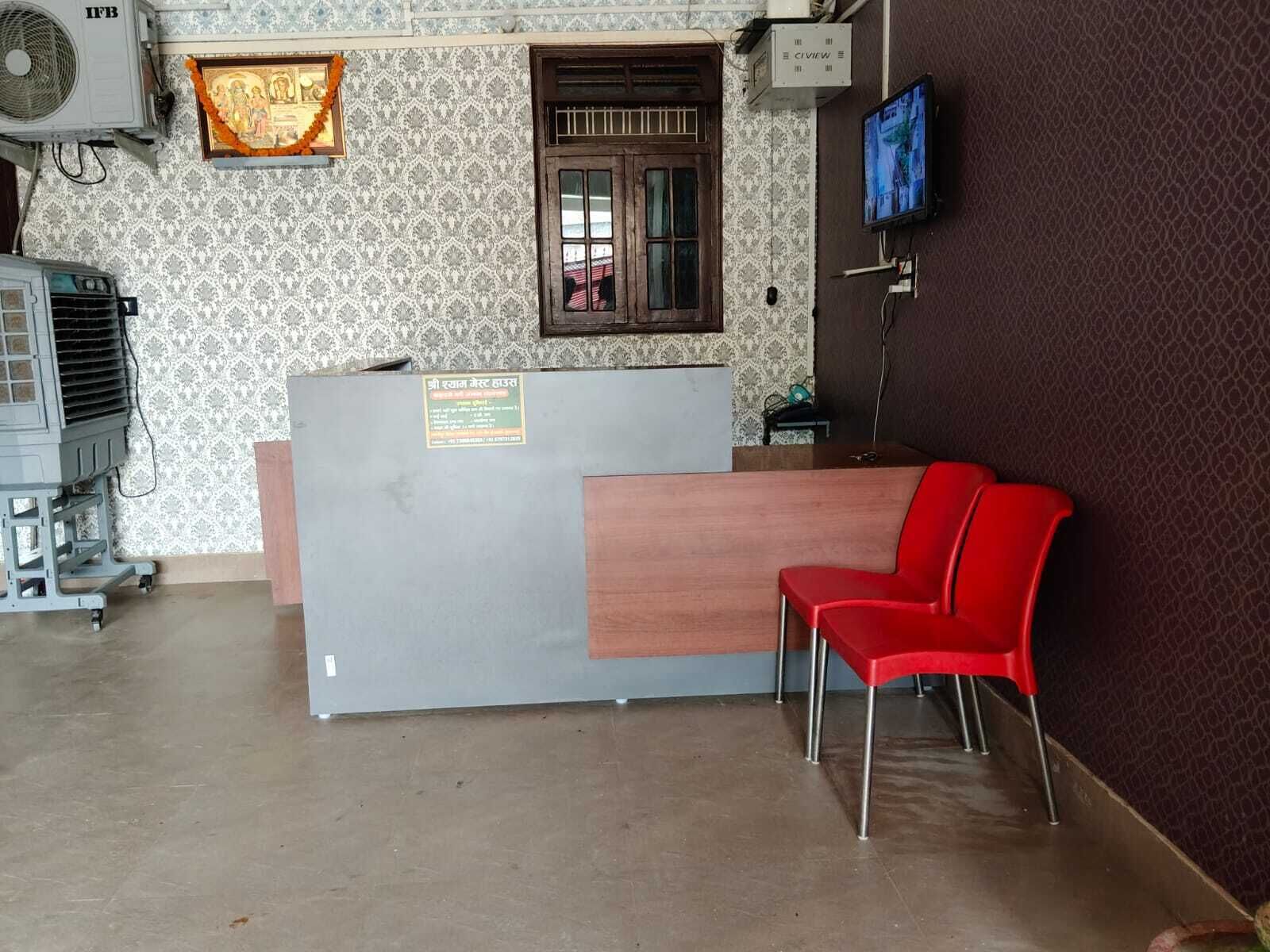 Uma área de recepção com balcão de madeira, uma cadeira vermelha, televisão na parede e papel de parede estampado.