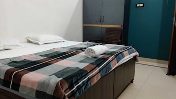 Cama bem arrumada com colcha xadrez e toalha enrolada, guarda-roupa de madeira e porta com puxador.