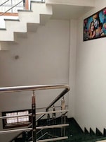 Uma escadaria com corrimão de metal, uma janela com grades e um quadro fixado na parede.