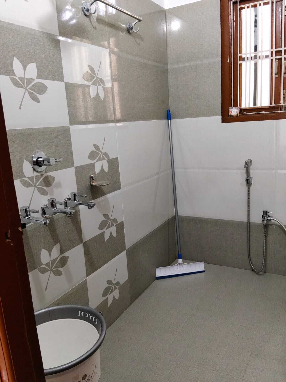 Casa de banho com chuveiro, sanita e um esfregão encostado na parede.