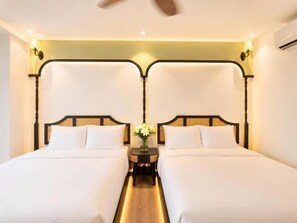 Quarto de hotel com duas camas, uma mesa de cabeceira entre elas e um ventilador de teto.