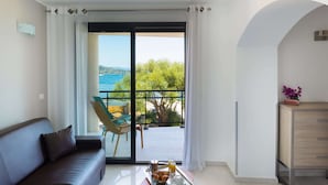 Sala de estar moderna com sofá, mesa de jantar com itens de café da manhã e vista para o mar por uma grande janela.