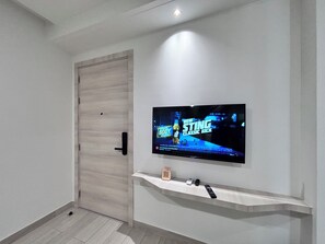 Um corredor moderno com uma porta, uma TV montada exibindo um anúncio e uma prateleira com um controle remoto.