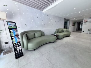Um lobby moderno com um sofá verde curvo, um quiosque de informações digital e uma parede com adesivos de pássaros.