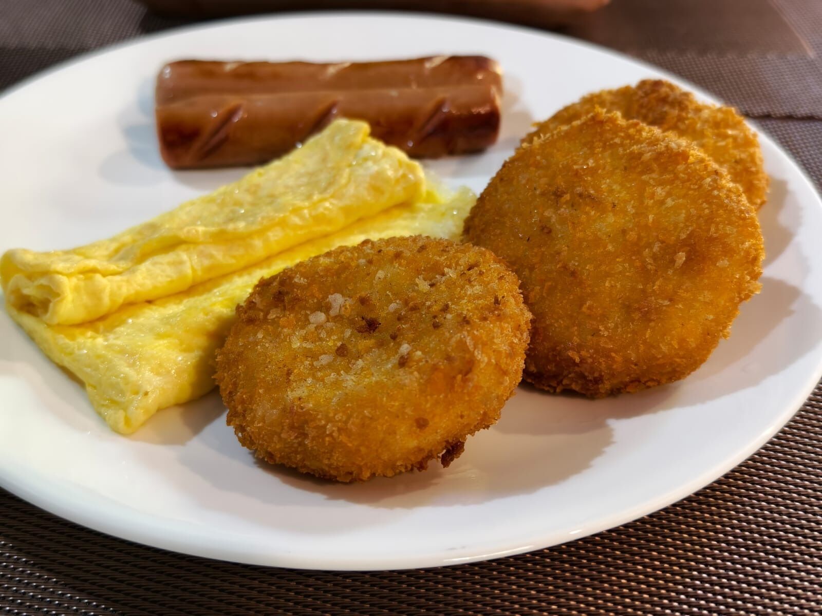 Um prato com dois alimentos fritos, um omelete dobrado e uma salsicha.