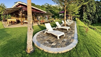 Um resort com área de estar coberta ao ar livre, cadeiras de descanso e gramado bem cuidado.