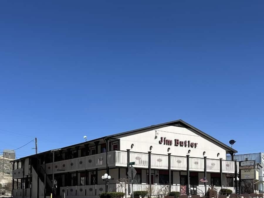 Um edifício de dois andares com a inscrição 'Jim Butler' na fachada, apresentando uma varanda no andar superior e um telhado plano.