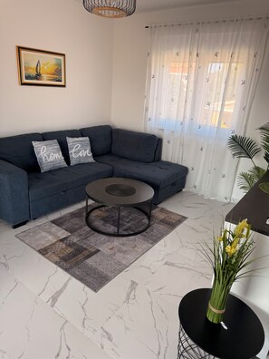 Sala de estar com sofá azul escuro, duas almofadas, mesa de centro redonda e um quadro na parede.