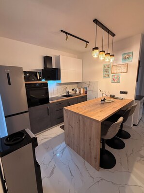 Cozinha moderna com bancada de mármore, forno embutido e geladeira de aço inoxidável.