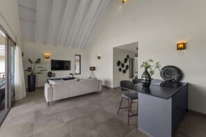 Uma sala de estar moderna com um sofá, uma mesa de jantar e uma televisão. Há luminárias decorativas na parede e um espelho grande.