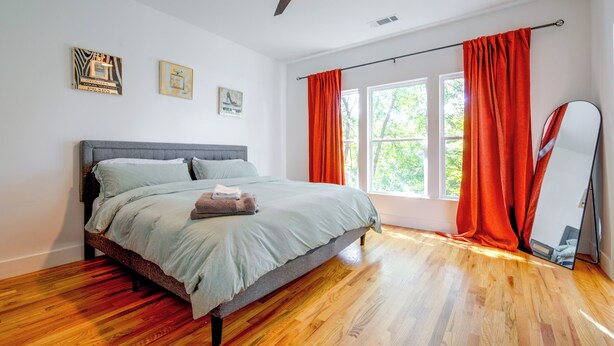 Quarto com cama, ventilador de teto, janela com cortinas e uma obra de arte na parede.