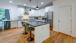 Cozinha moderna com ilha central, eletrodomésticos de aço inoxidável e iluminação pendente.