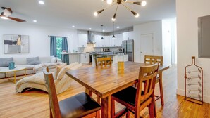 Cozinha moderna com armários brancos, ilha central e área de jantar com mesa e cadeiras de madeira.