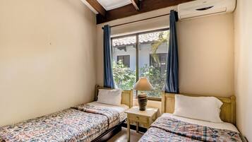 Quarto com duas camas de solteiro, uma mesinha com abajur e uma janela com cortinas.