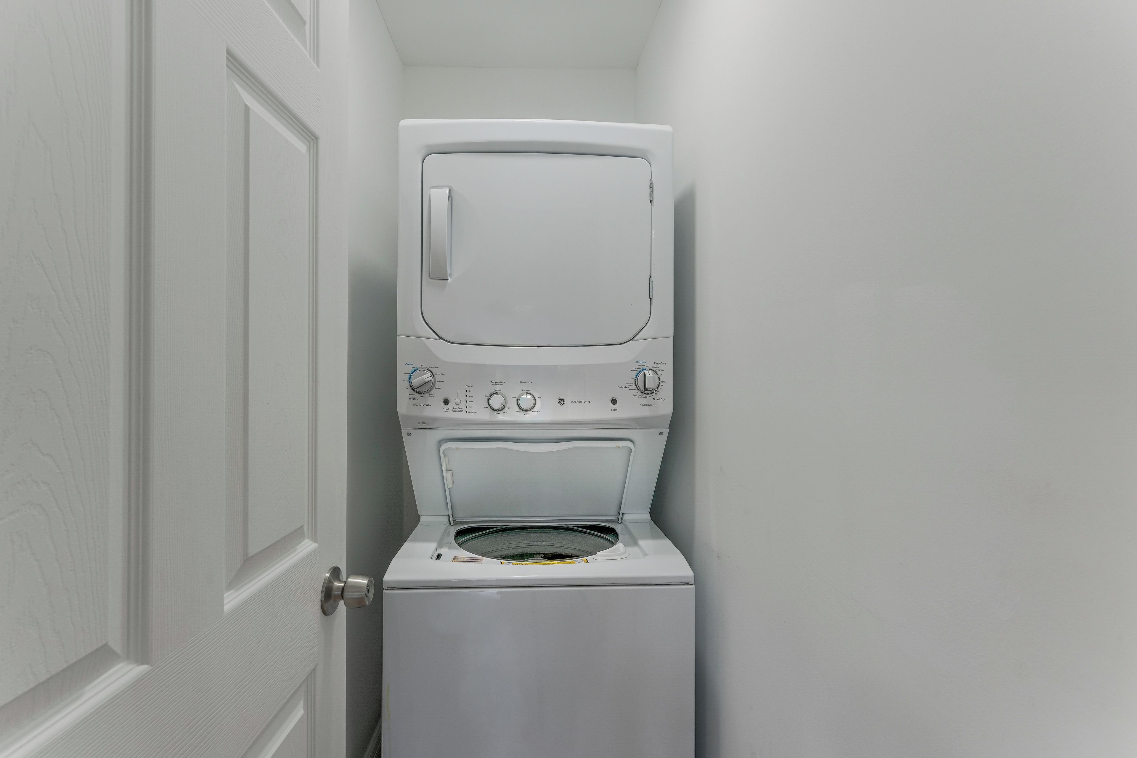 Máquina de lavar roupa compacta e branca, de abertura frontal, numa lavanderia pequena com porta fechada.