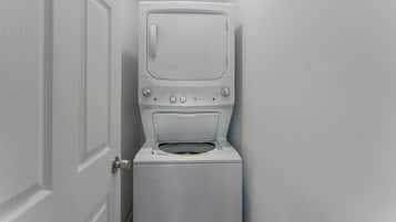 Máquina de lavar roupa compacta e branca, de abertura frontal, numa lavanderia pequena com porta fechada.