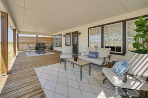 Uma área de pátio coberta com deck de madeira, mobiliário de exterior e grandes janelas.