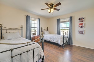 Quarto com duas camas, ventilador de teto e janela com cortinas.