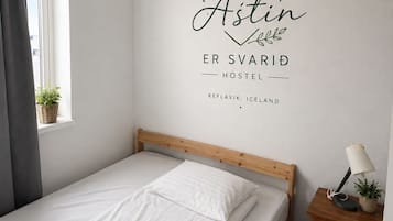 Quarto minimalista com uma cama, mesa de cabeceira com abajur e uma decoração na parede.