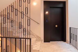 Uma escadaria com design moderno, uma porta escura e um lustre.