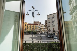 Vista de uma rua da cidade vista da janela, com edifícios, um lampião e carros estacionados.