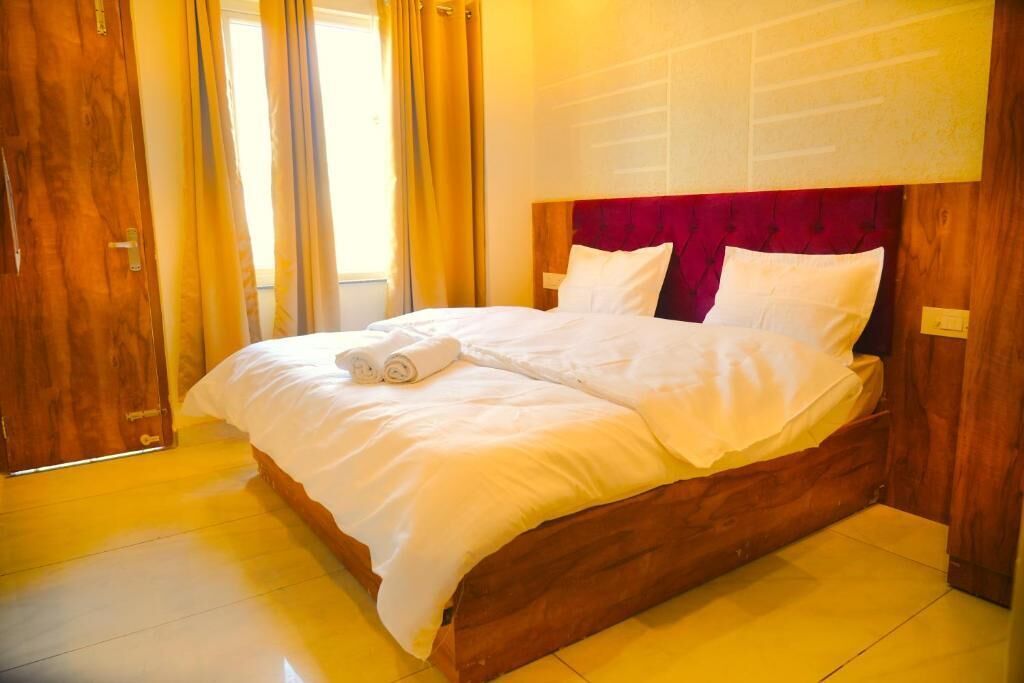 Quarto de hotel com estrutura de cama de madeira, roupa de cama branca e cabeceira vermelha.