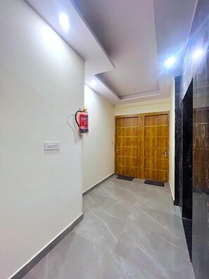 Corredor com extintor, porta de madeira e chão de azulejos.