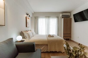 Quarto com cama, mesa de cabeceira com abajur, guarda-roupa e TV fixada na parede.