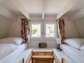 Quarto pequeno e triangular com duas camas, janela e aquecedor.