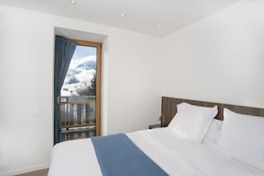 Quarto com cama, mesa de cabeceira e janela com vista para montanhas.