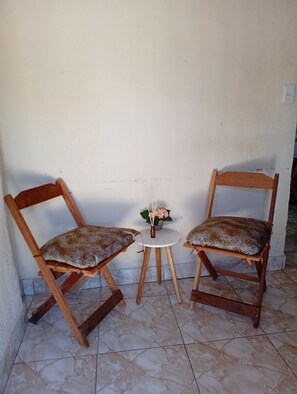 Duas cadeiras de madeira com assentos acolchoados e uma pequena mesa redonda com um vaso de flores.