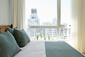 Quarto de hotel com cama, cortinas e vista para edifícios da cidade.