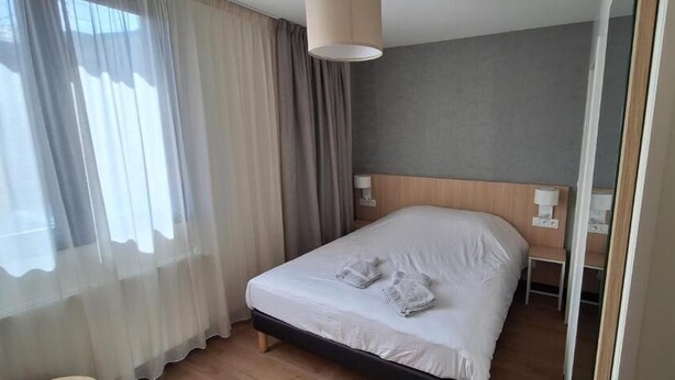 Quarto de hotel com cama, cortinas, cabeceira e mesa de cabeceira.