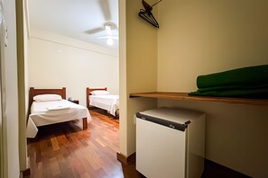 Quarto pequeno com duas camas, ventilador de teto e um refrigerador compacto.
