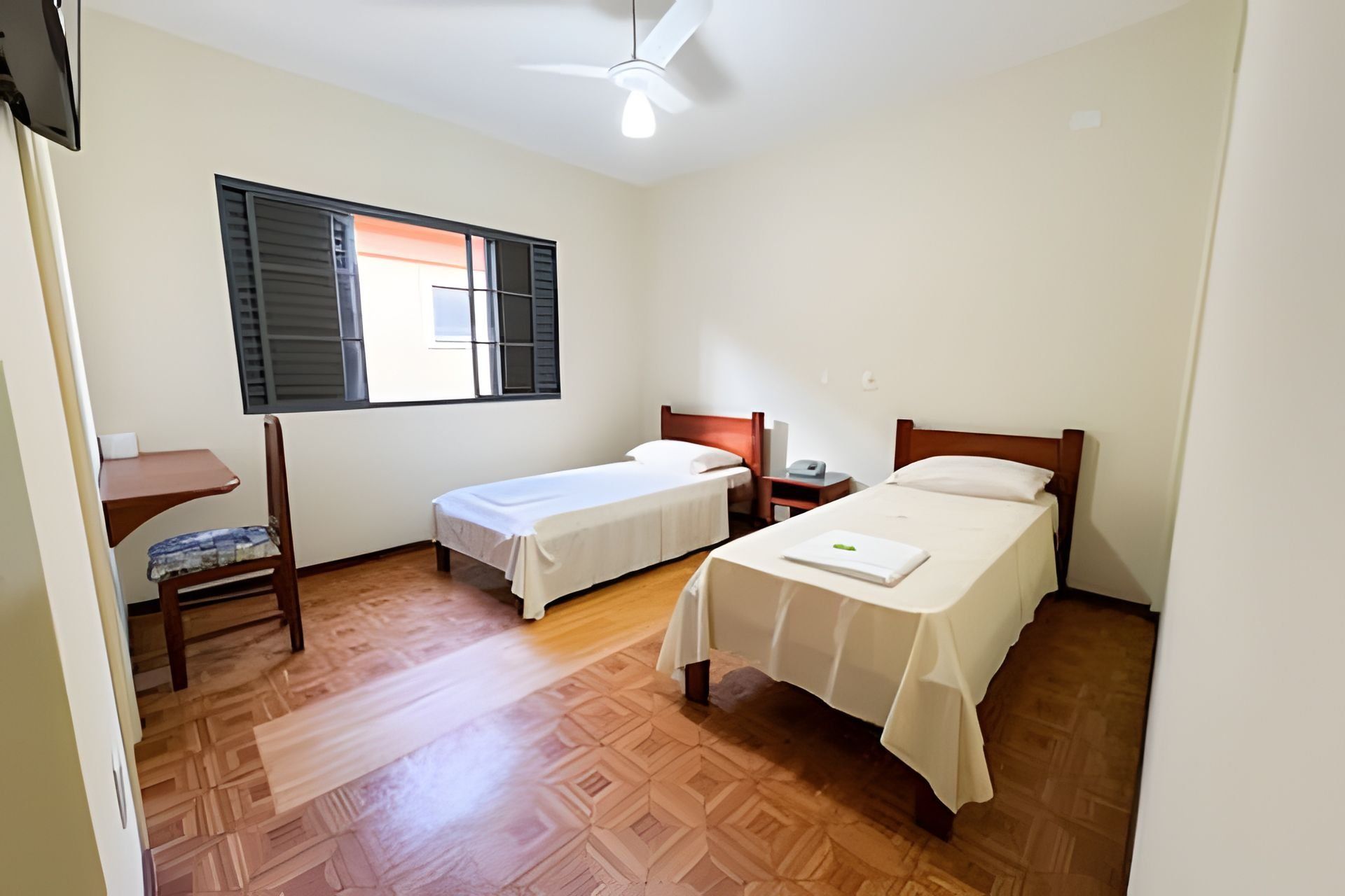 Quarto com duas camas de solteiro, uma escrivaninha e uma cadeira.