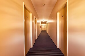 Corredor de hotel com portas em ambos os lados, piso coberto de carpete e luminária no teto.