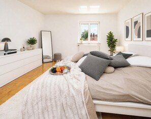 Quarto com cama, mesa de cabeceira, luminária, espelho e janela com vista.