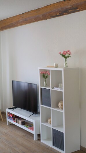 Uma unidade de entretenimento branca com uma TV de tela plana, prateleiras e objetos decorativos, incluindo um vaso com flores.