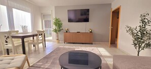 Uma sala de estar moderna com área de jantar, televisão de tela plana na parede e um vaso de planta.