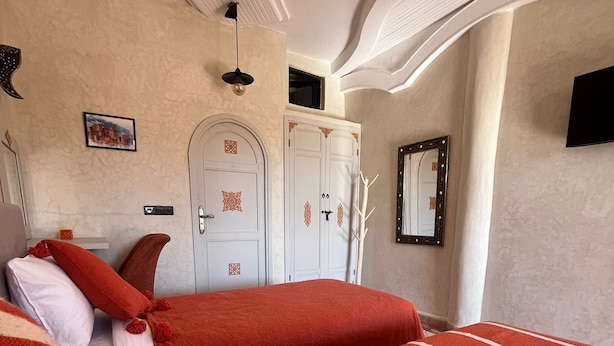 Quarto de hotel com cama, duas portas brancas, espelho e televisão fixada na parede.