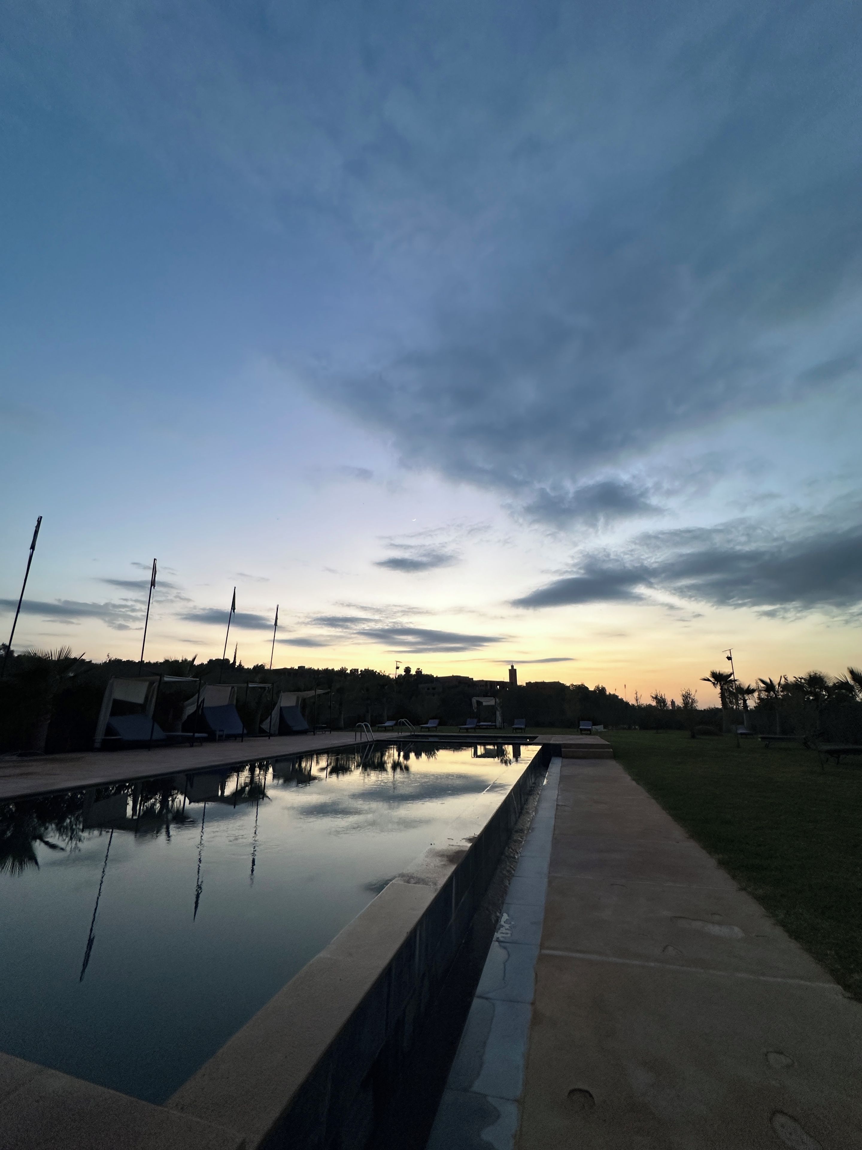 Piscina com espreguiçadeiras e céu ensolarado.