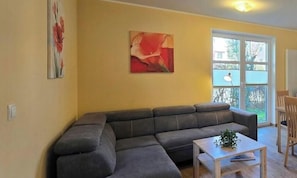 Uma sala de estar com sofá seccional, mesa de centro e duas pinturas na parede.