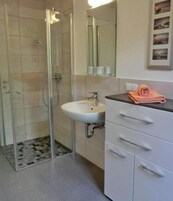 Casa de banho com cabine de duche em vidro, lavatório e toucador com gavetas.