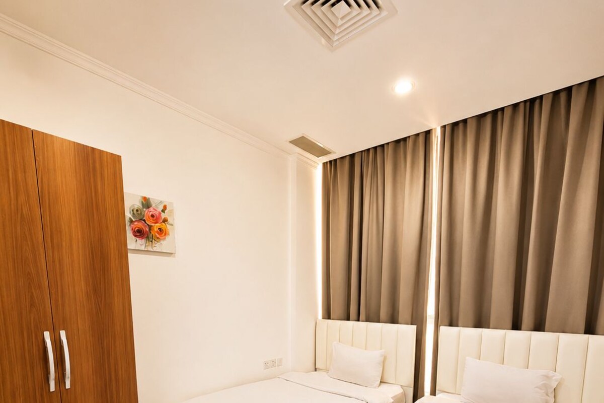 Quarto de hotel com duas camas, um guarda-roupa de madeira e um respiradouro no teto.